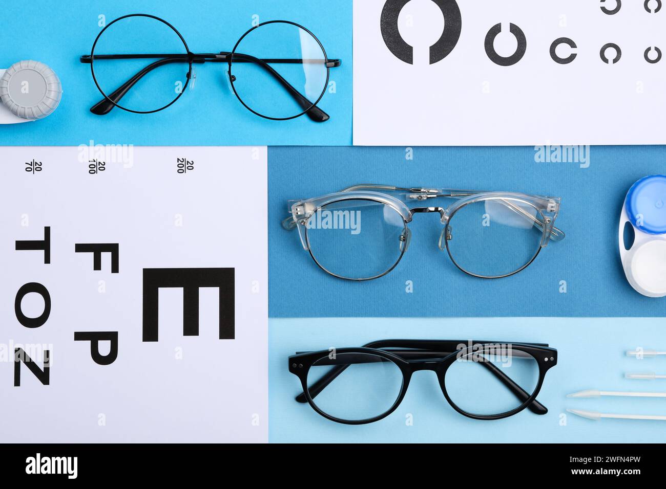 Vision test charts, glasses, lenses and tweezers on light blue ...