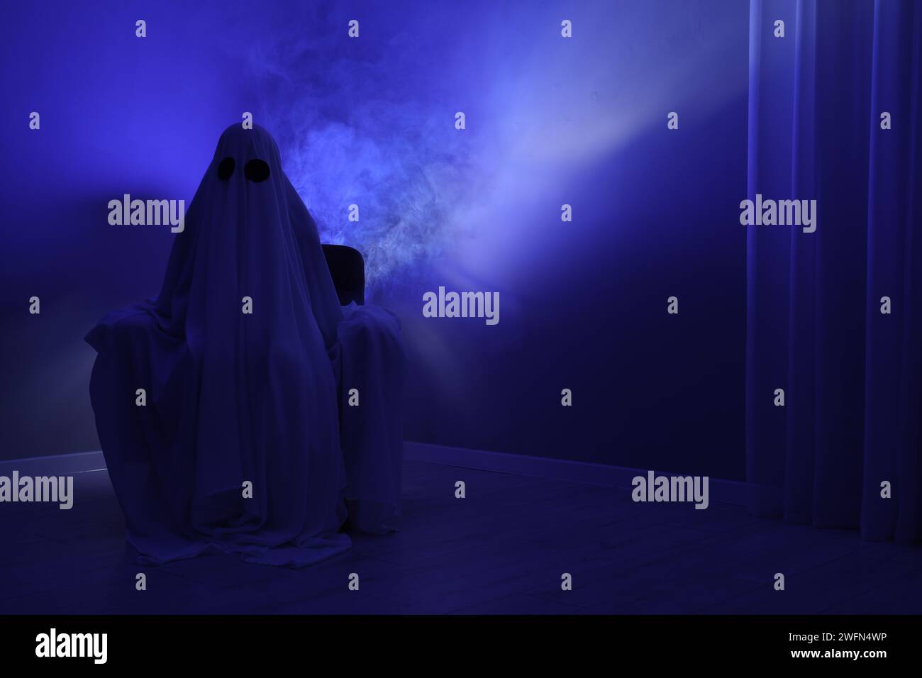 Creepy ghost. Woman covered with sheet sitting in armchair in blue ...