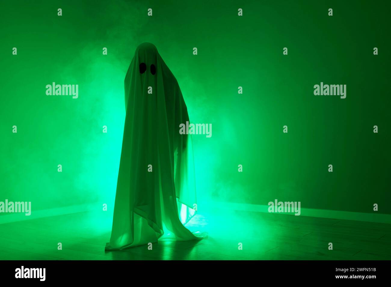 Creepy ghost. Woman covered with sheet in green light, space for text ...