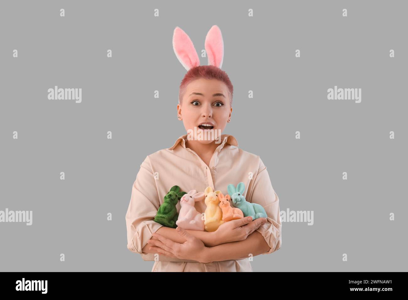Shocked young woman with bunny ears and Easter rabbits on grey ...
