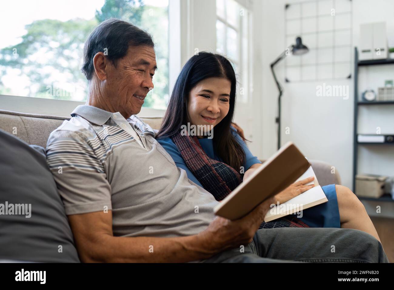 Retired elderly couple sits on couch in their home reading relaxing book. Senior Activity ...