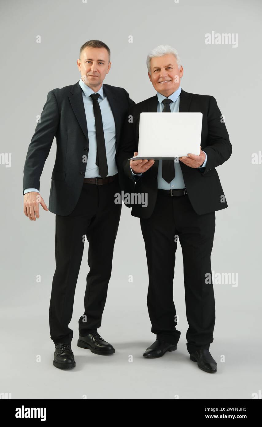 Mature brothers in suits with laptop on grey background Stock Photo - Alamy