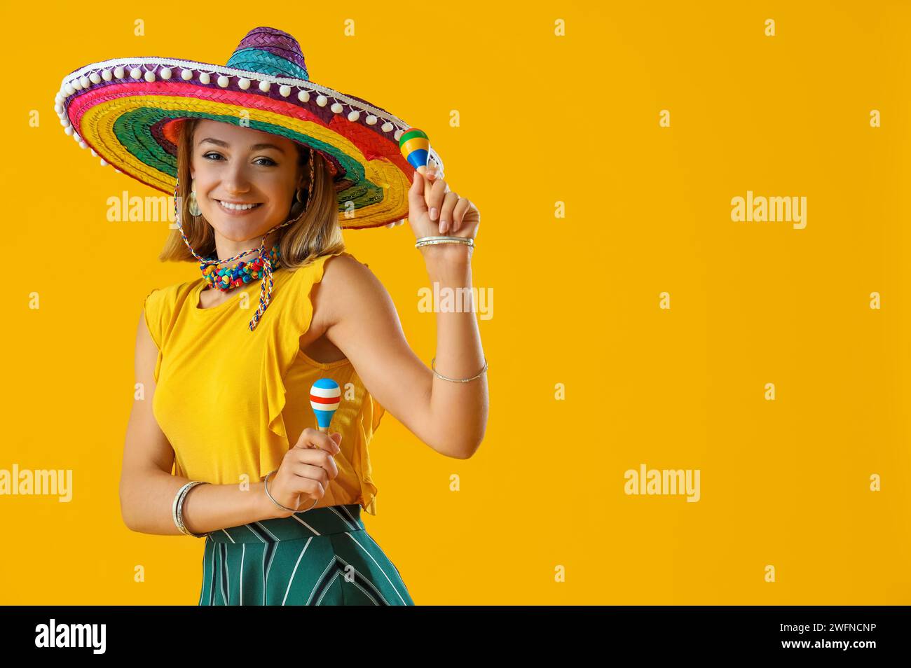 Pretty young woman in sombrero dancing with maracas on yellow ...