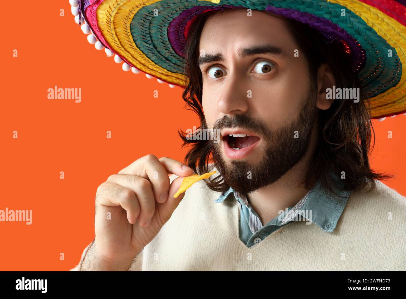Surprised young Mexican man in sombrero eating nachos on orange ...
