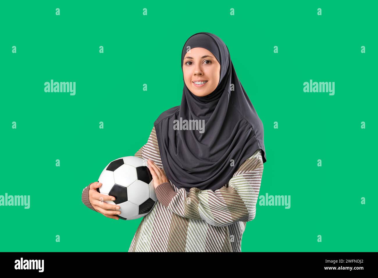 Young beautiful Muslim woman in hijab with soccer ball on green ...