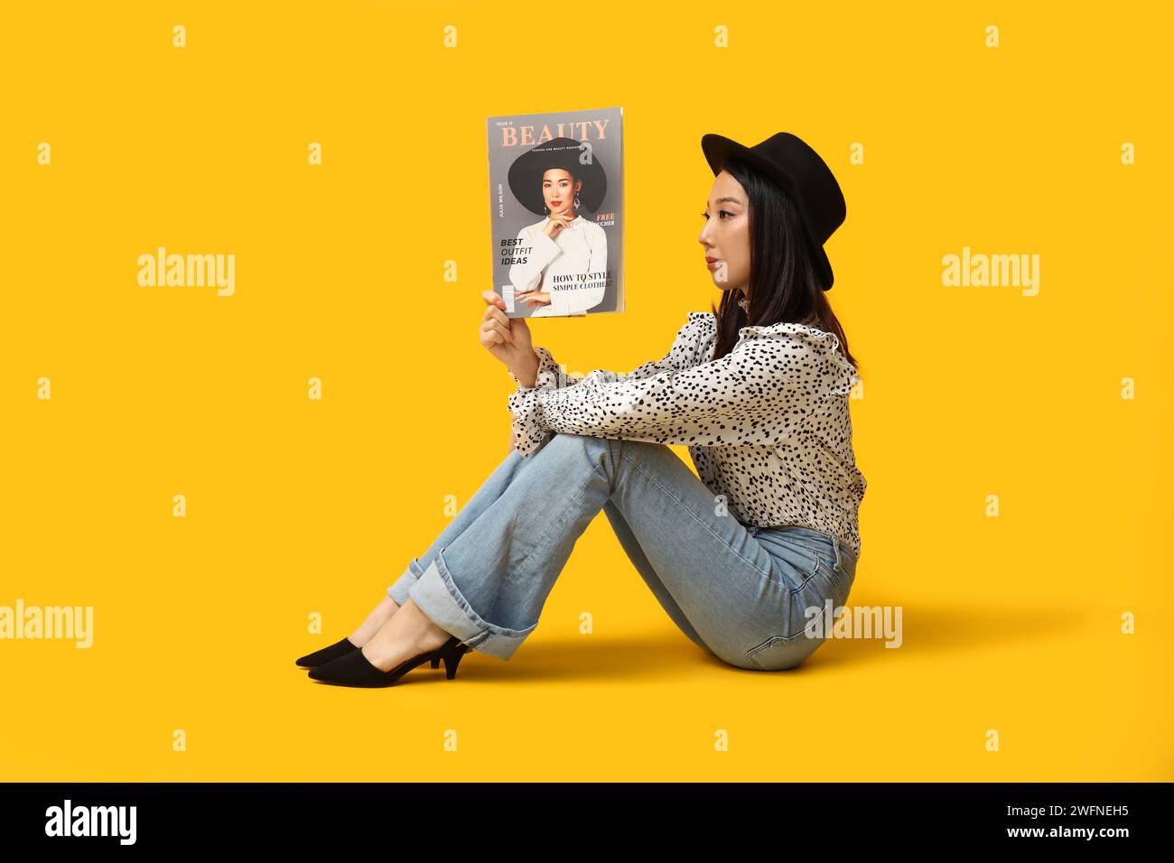 Beautiful young Asian woman in stylish jeans with magazine sitting on ...