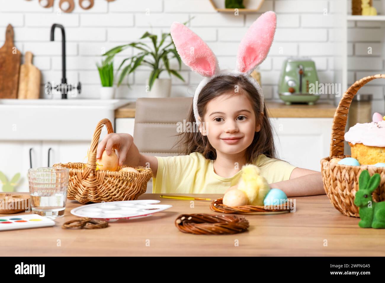 Cute little girl with bunny ears putting Easter eggs in wicker baskets ...