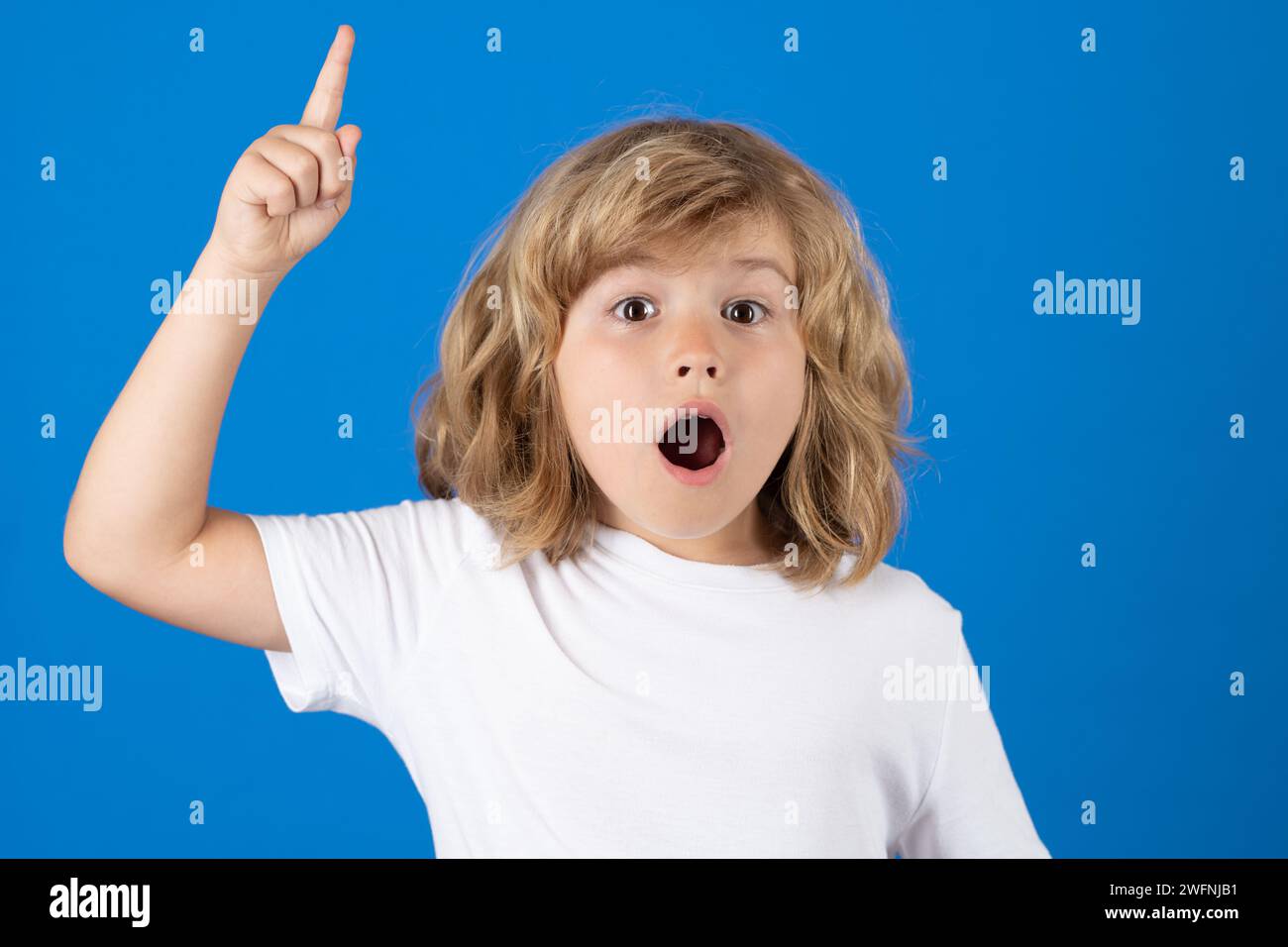 Surprised kid pointing up finger on blue background. Shocked kid ...