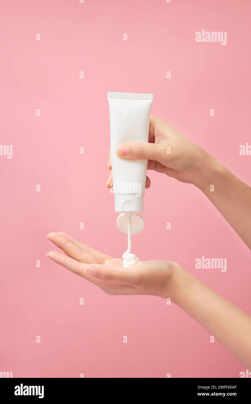 Over a pink background, a hand model squeezing cream from a white ...