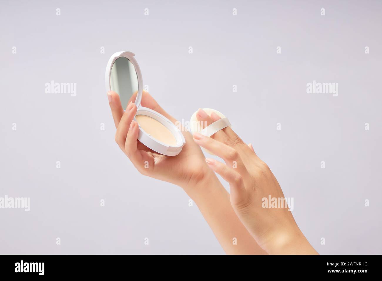 A compact powder with a makeup puff displayed on female hand model over ...