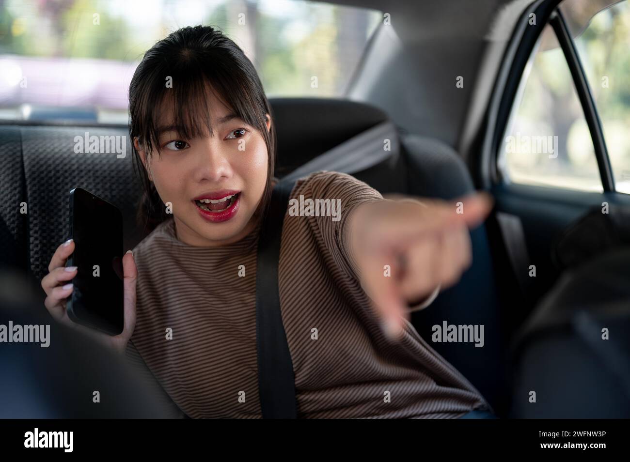 A happy young Asian female passenger is giving directions to a taxi ...