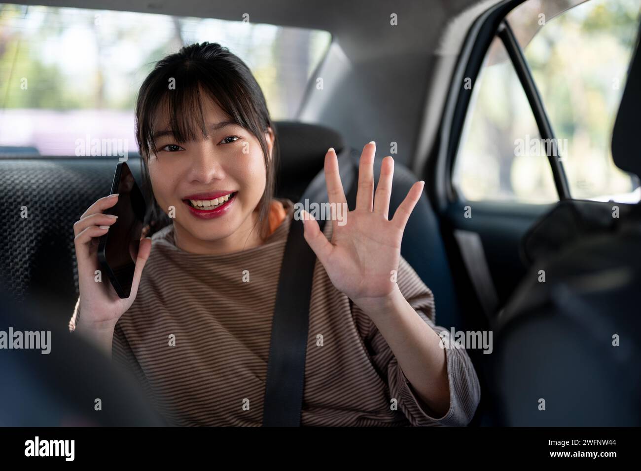 A happy young Asian female passenger is giving directions to a taxi ...