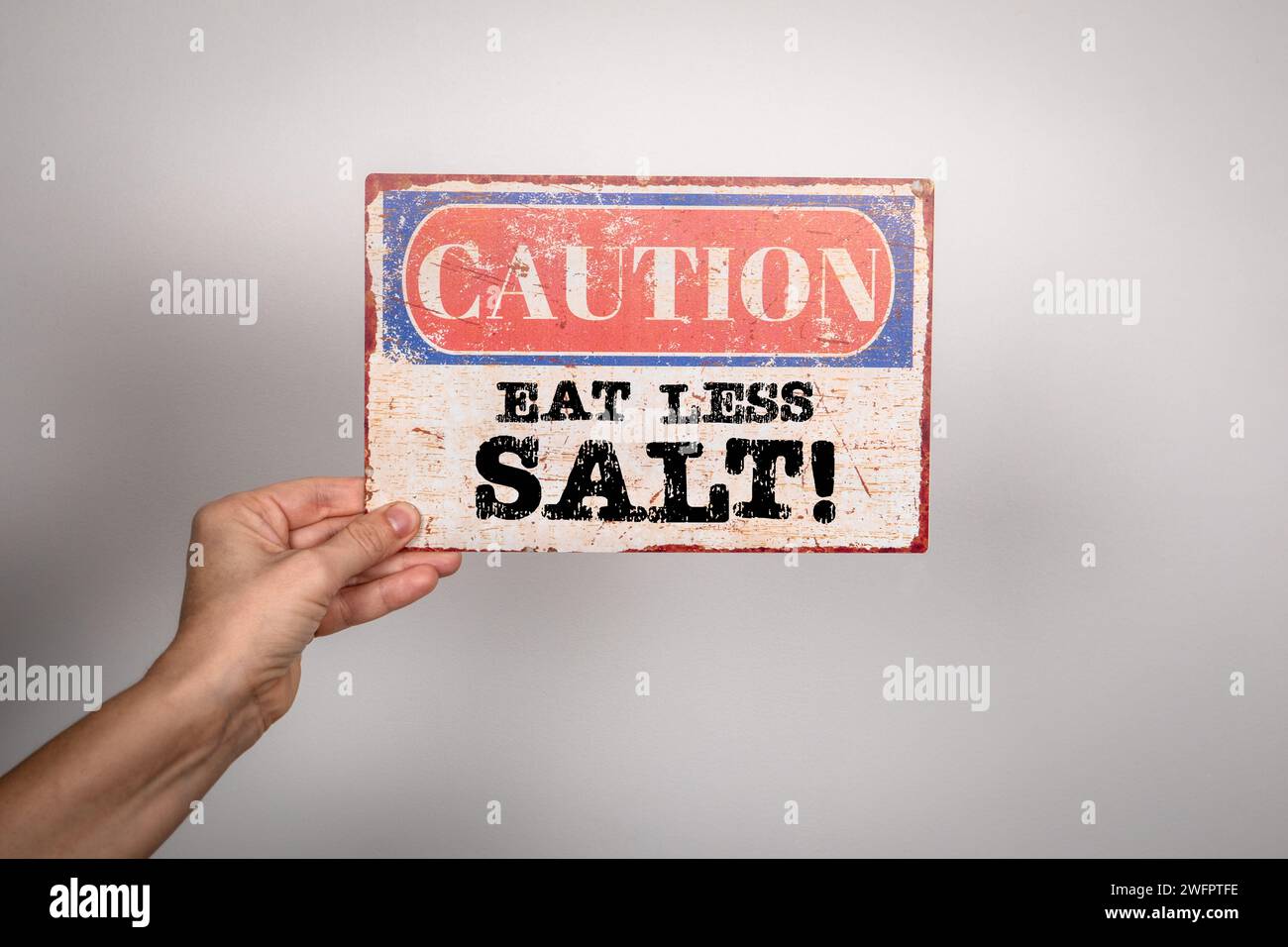 Eat Less Salt. Metal warning sign in a woman's hand on a white ...