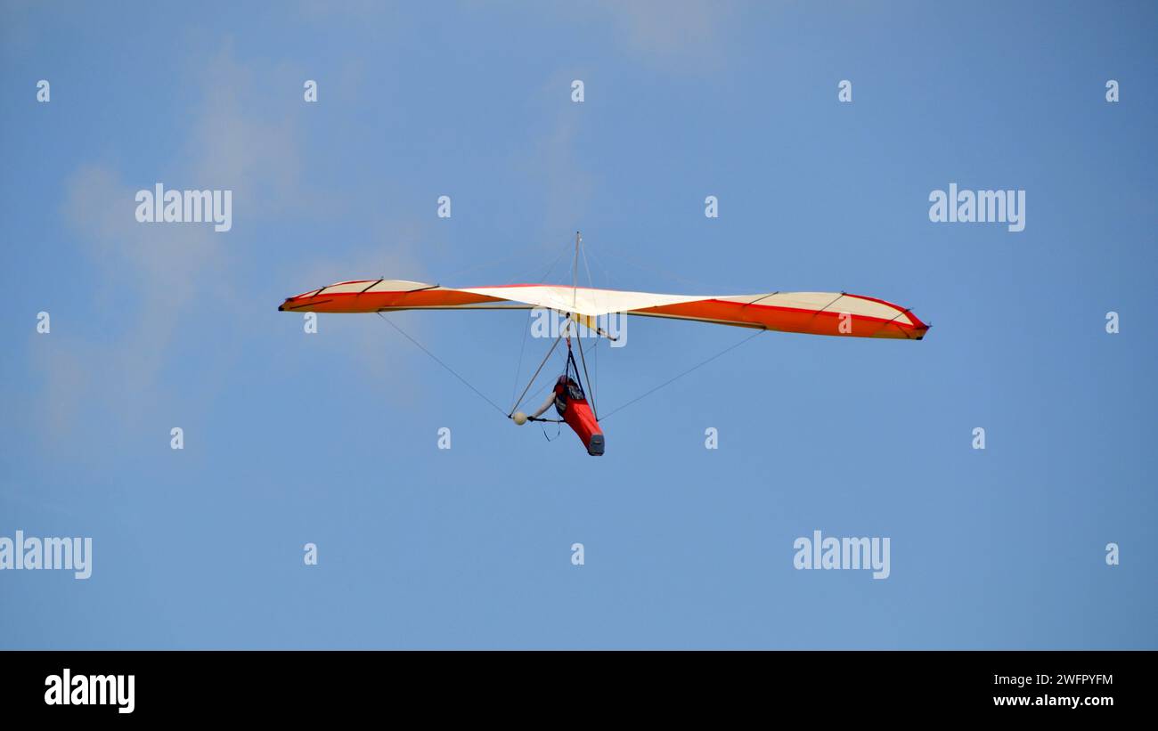 Red and white wing hang glider flying against a blue sky is an example ...