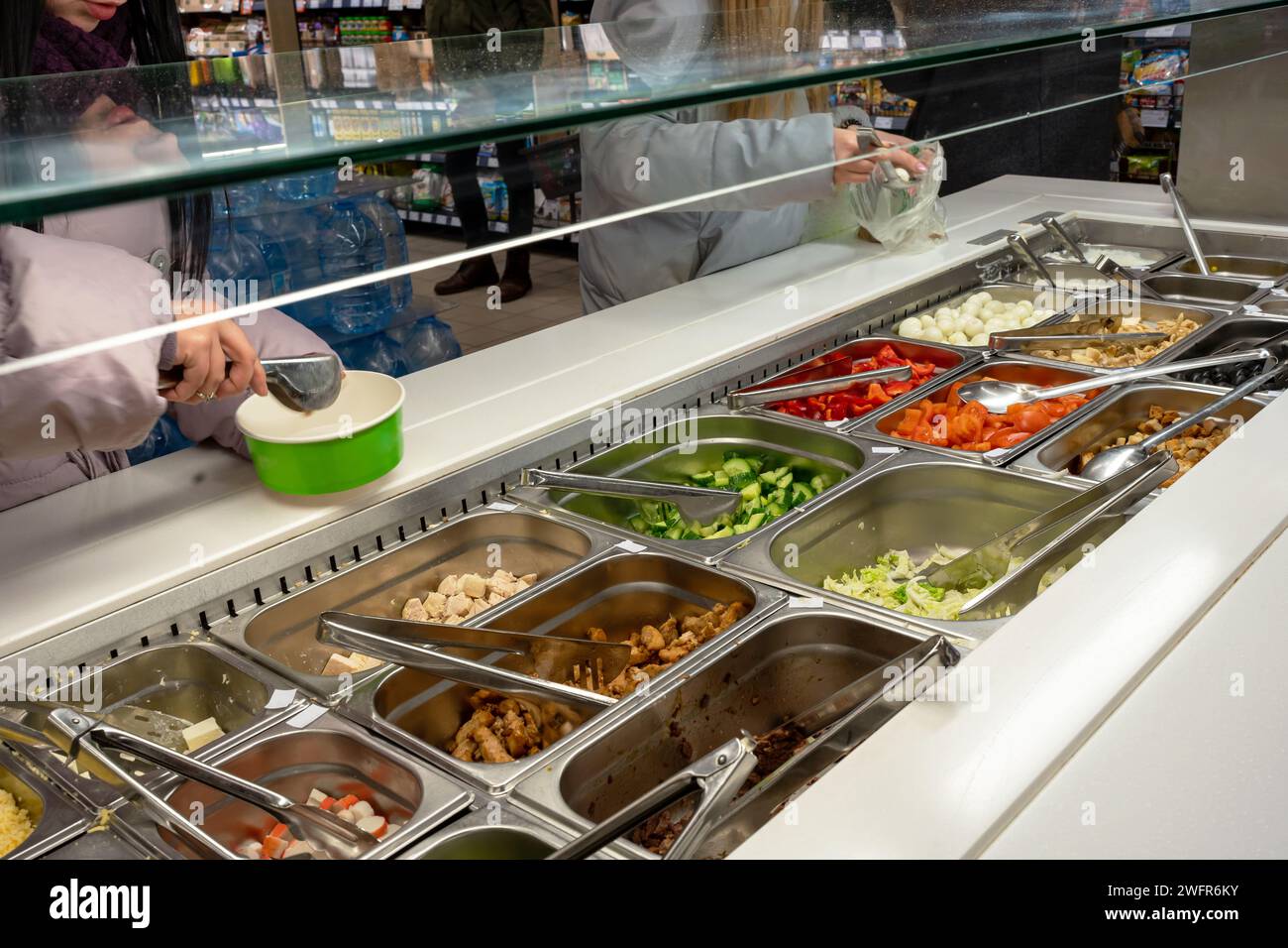 Fresh Salad bar counter with person's hands lifting vegetable into a ...