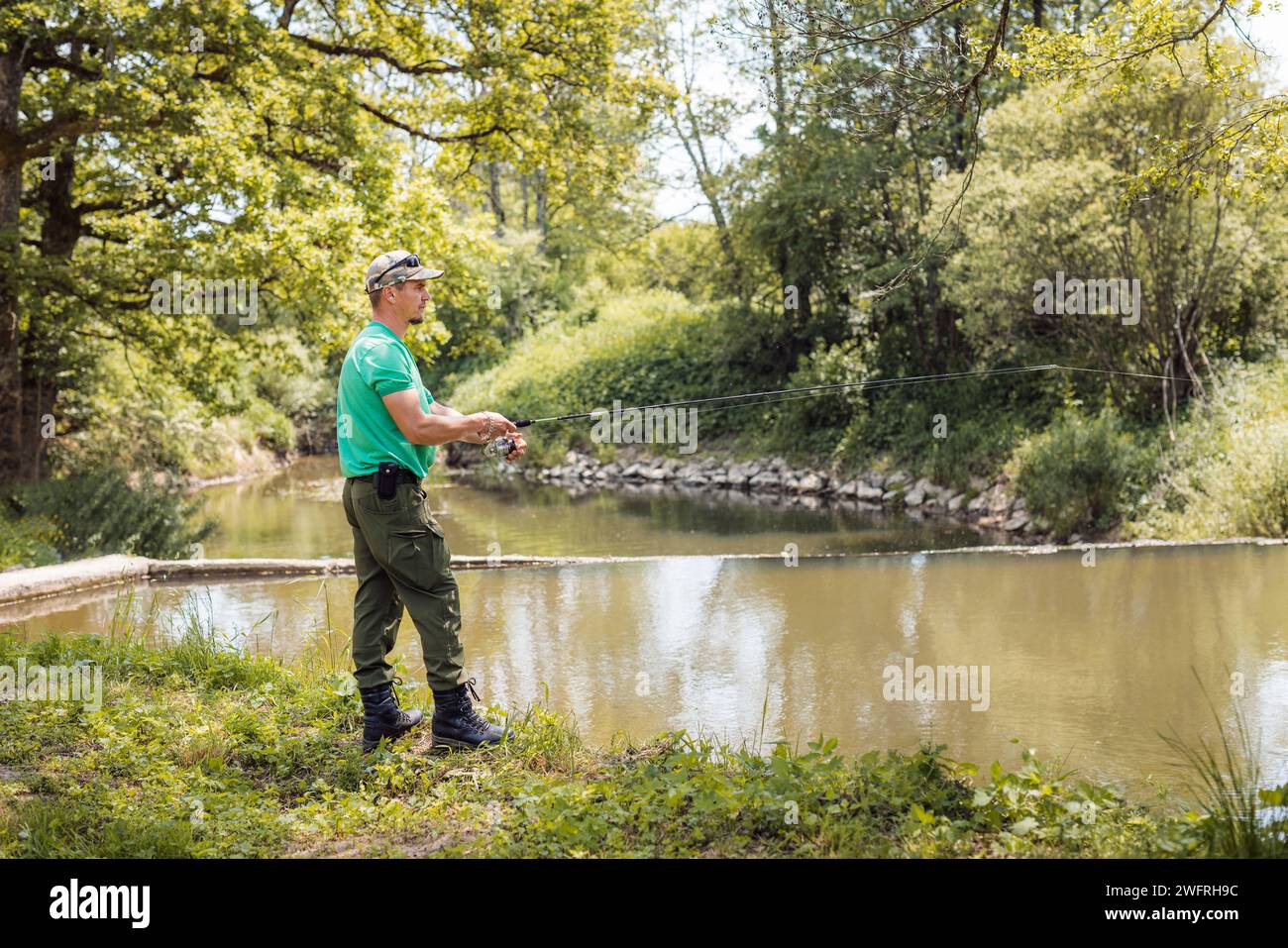 Young fisherman fishing on the river bank surrounded by beautiful green ...