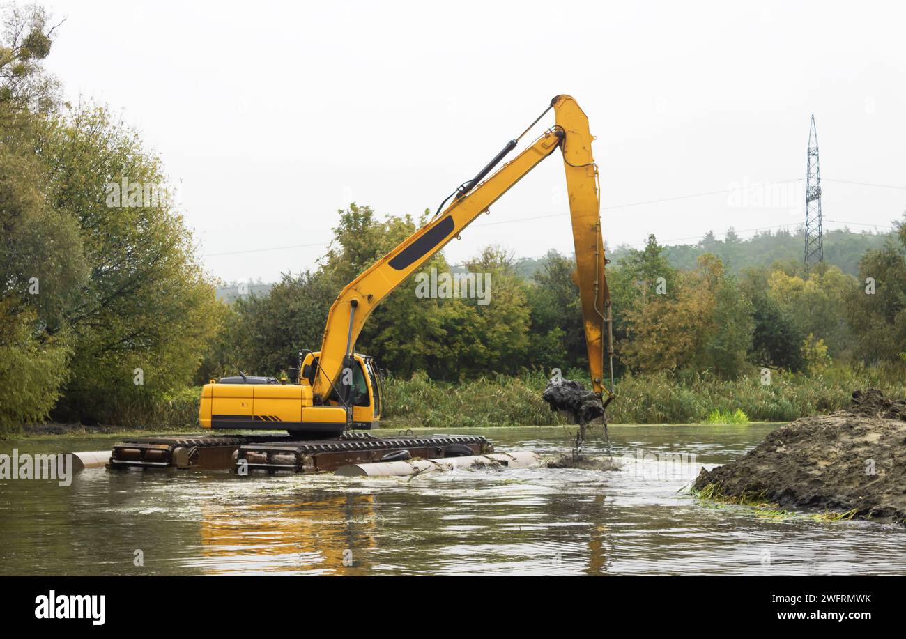 Yellow bulldozer on the water digs the river to deepen and clear the ...