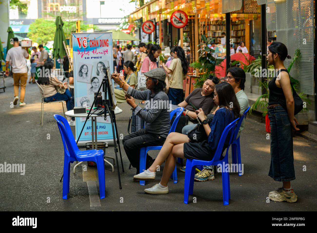 A Vietnamese street artist with customers om Book Street, Ho Chi Minh ...