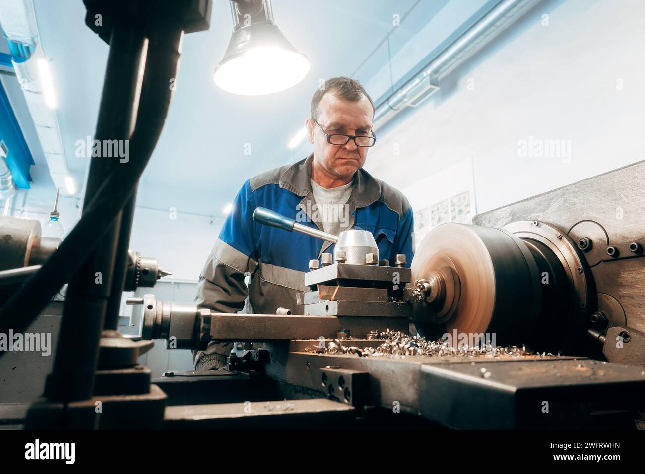 Elderly turner, 50-55 years old, works at lathe in turning shop. Front ...