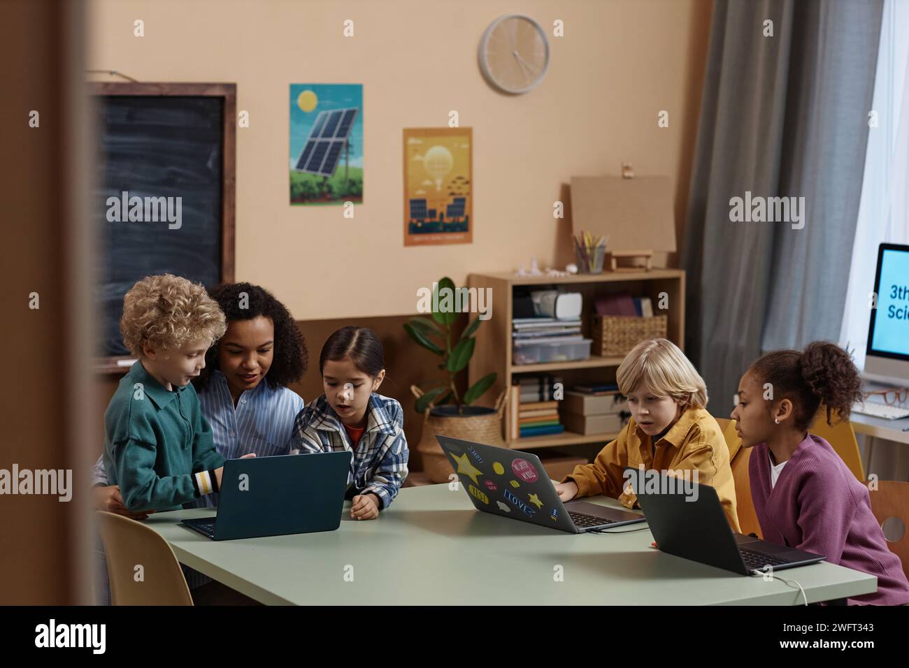 Diverse group of little children using computers at table in school ...