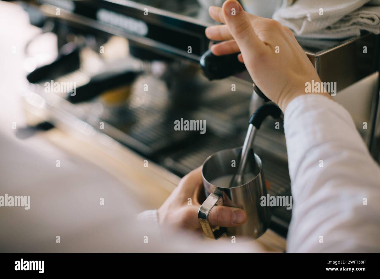 A barista prepares milk for cappuccino using an espresso machine. Close-up of a man preparing ...