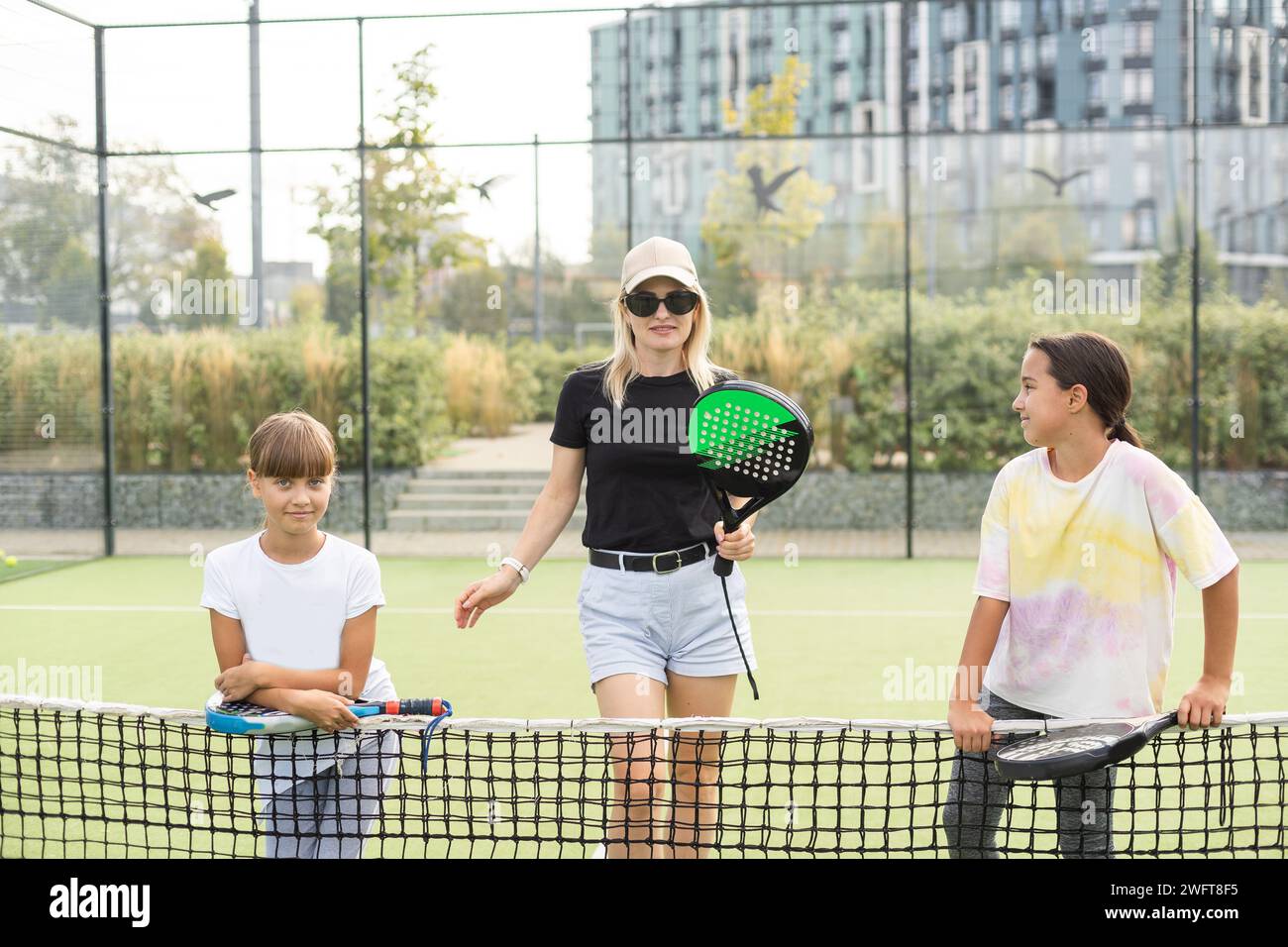 Young sporty woman with children playing padel game in court on sunny ...