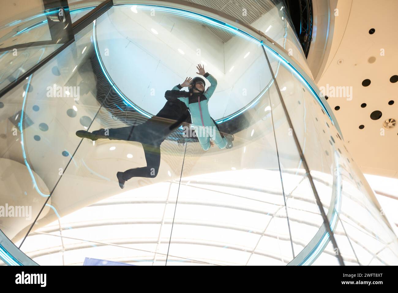 Excited teenage girl in helmet flying in aerodynamic tube wind tunnel ...