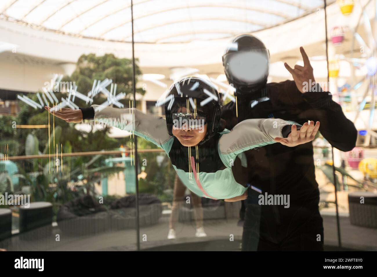 Excited teenage girl in helmet flying in aerodynamic tube wind tunnel ...