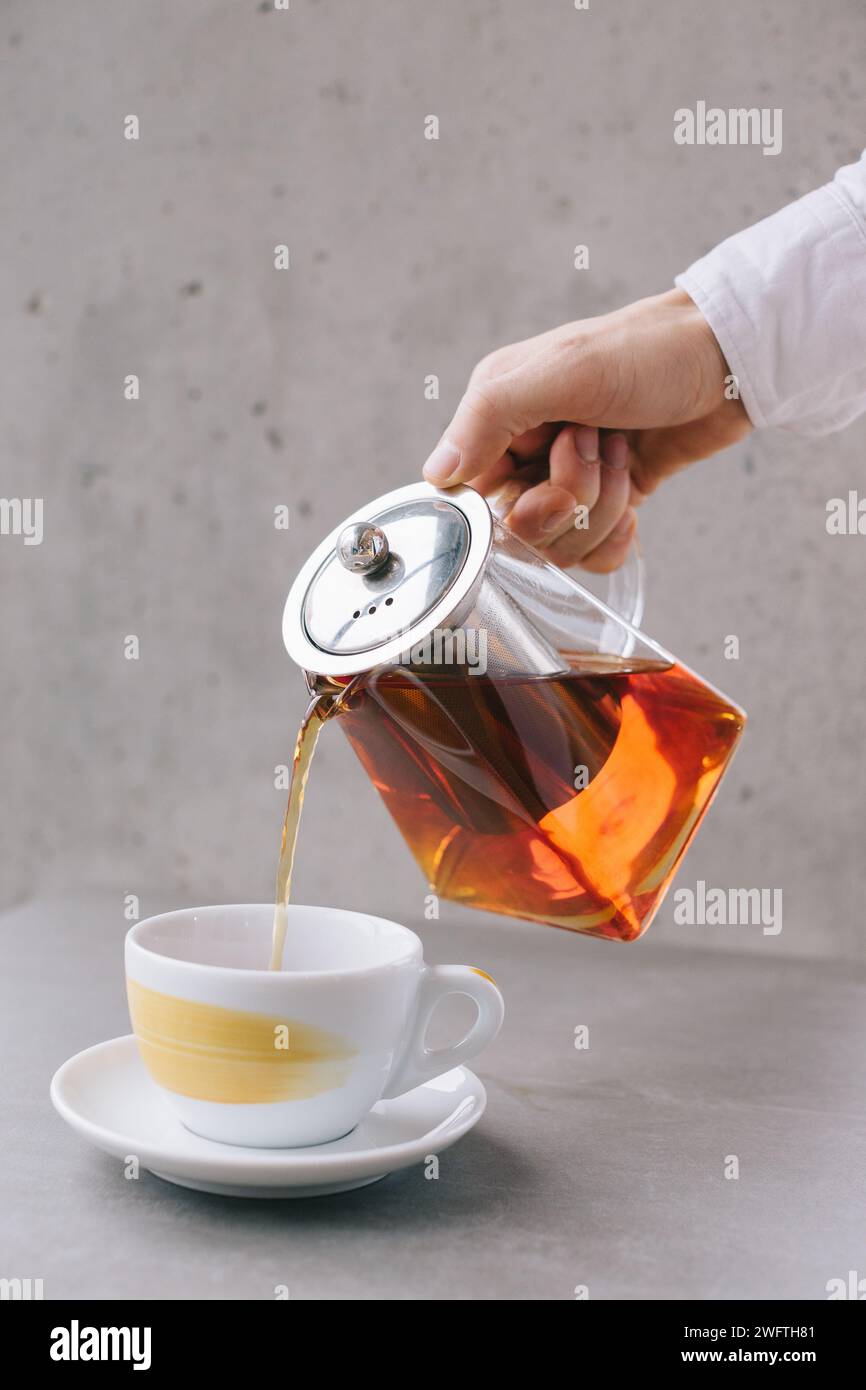 A barista's hand pours aromatic tea into a cup, isolated on a gray ...