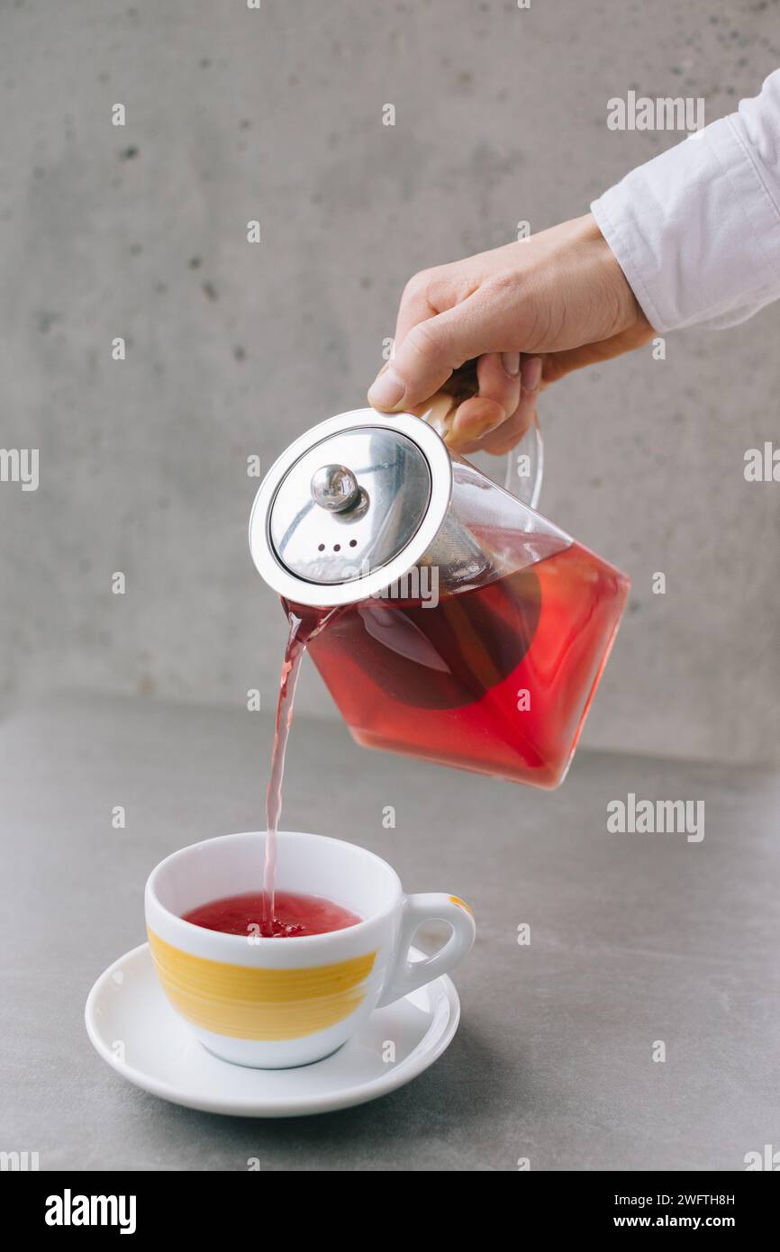 A barista's hand pours aromatic tea into a cup, isolated on a gray ...
