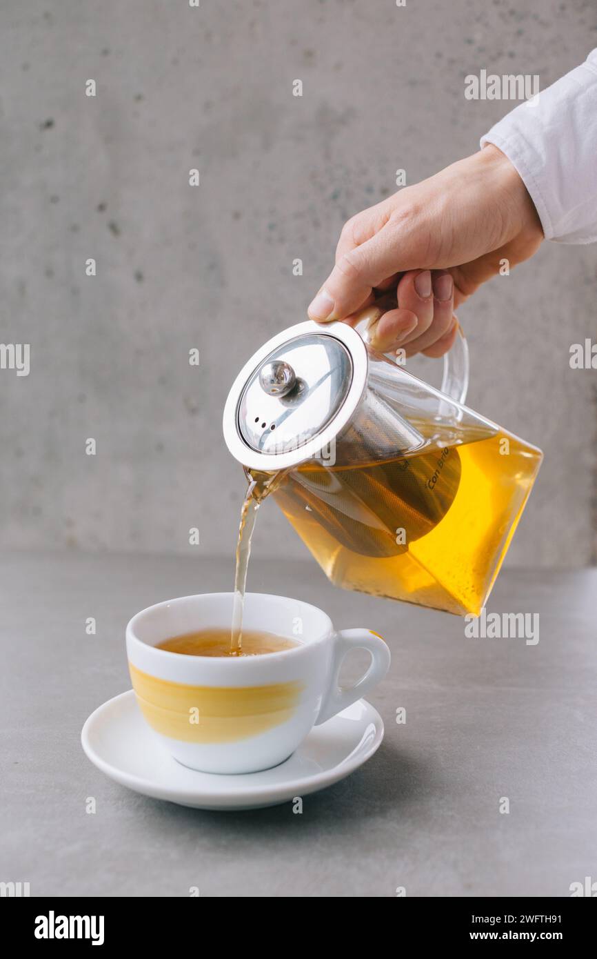 A barista's hand pours aromatic tea into a cup, isolated on a gray ...