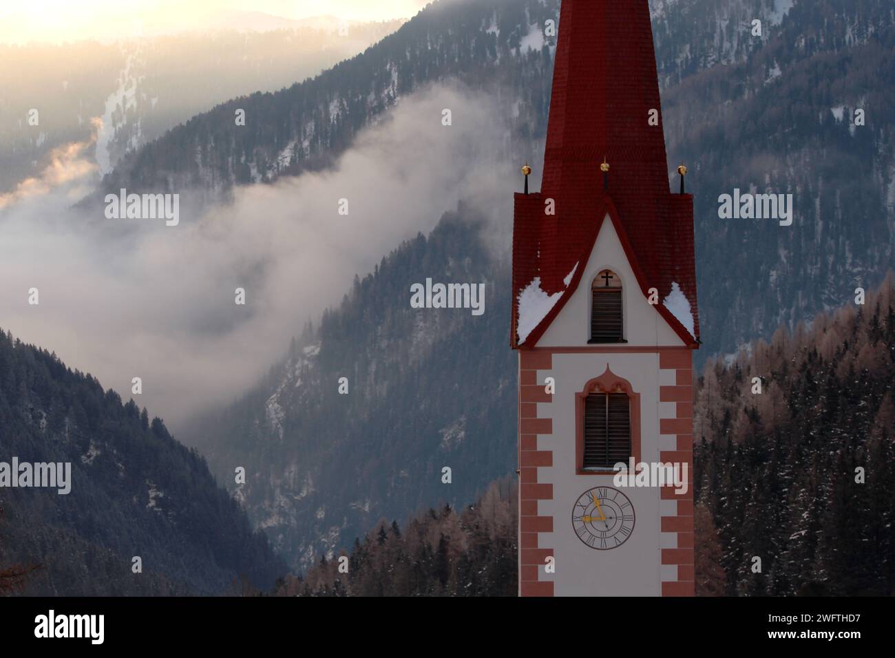 Church tower in Alps village. Great clouds go down from mountain peaks ...