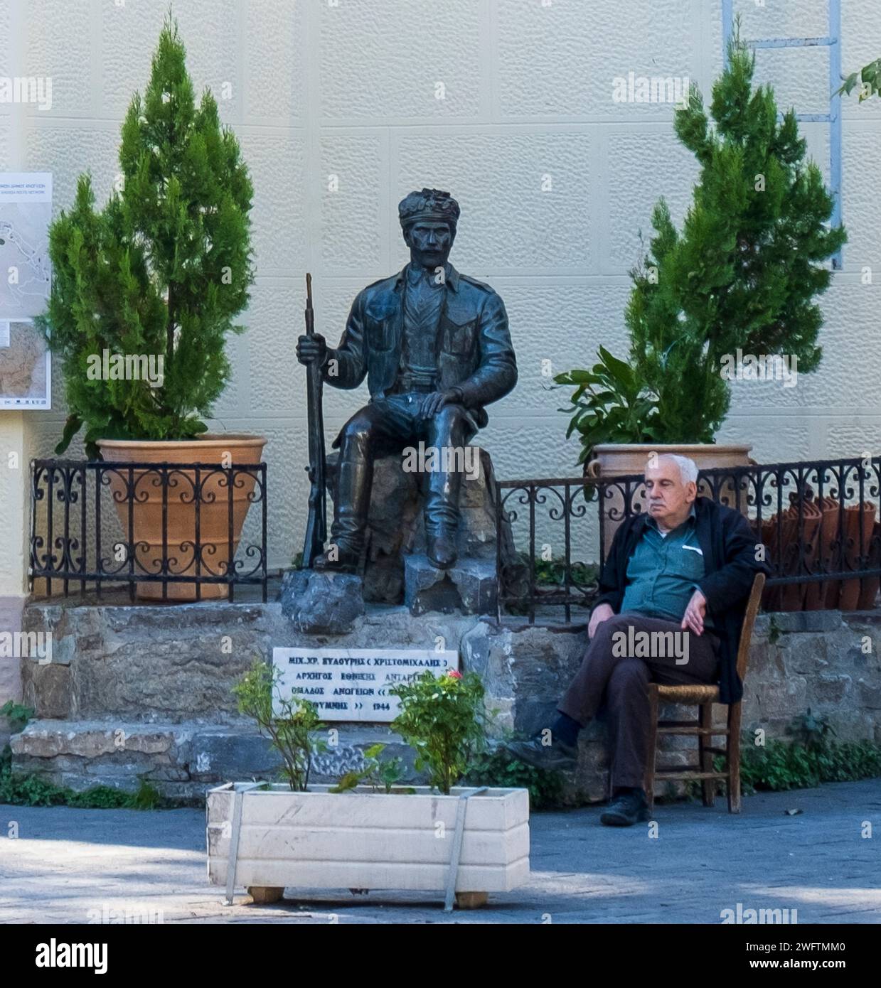 Elderly man sitting next to statue of Cretan freedom fighter in village ...