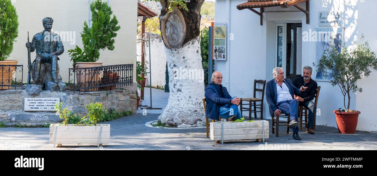Men sitting in village square next to statue of Cretan freedom fighter ...