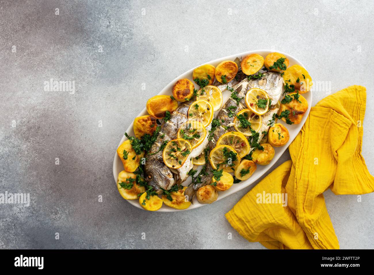 Oven-baked Dorada fish with potatoes and lemon slices, sprinkled with ...