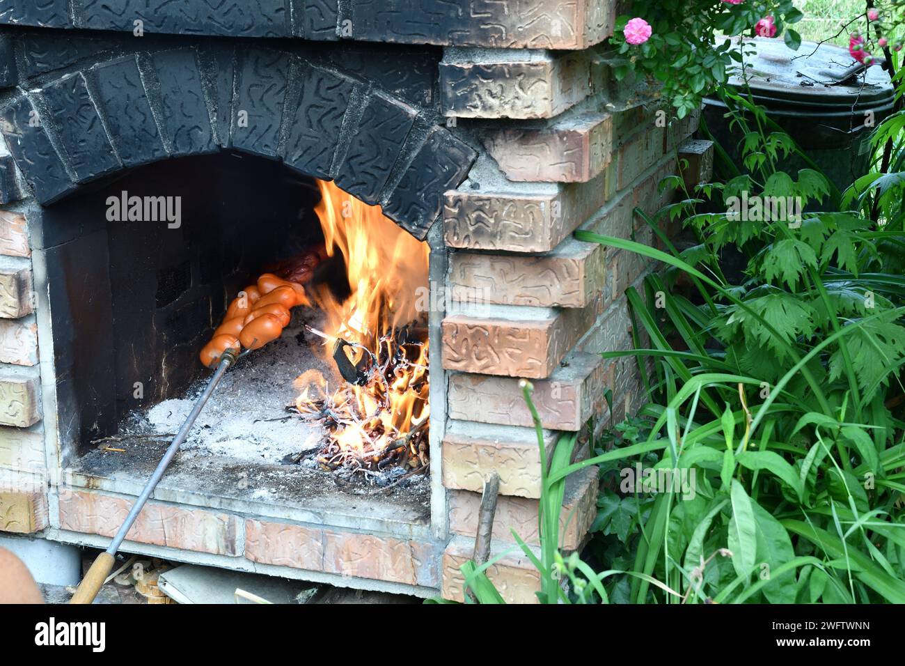 Man roasts meat sausages in a brick fireplace at the cottage Stock ...