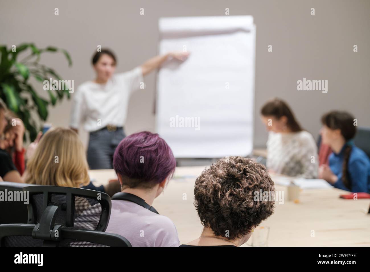 Rear view of a diverse audience focused on a female speaker at a ...