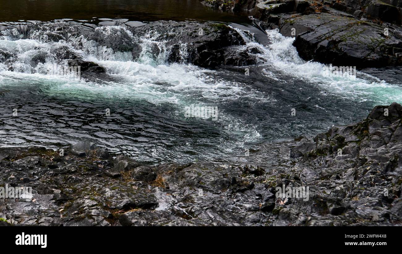 Turbulent white and teal river water rushing over black rocks Stock ...