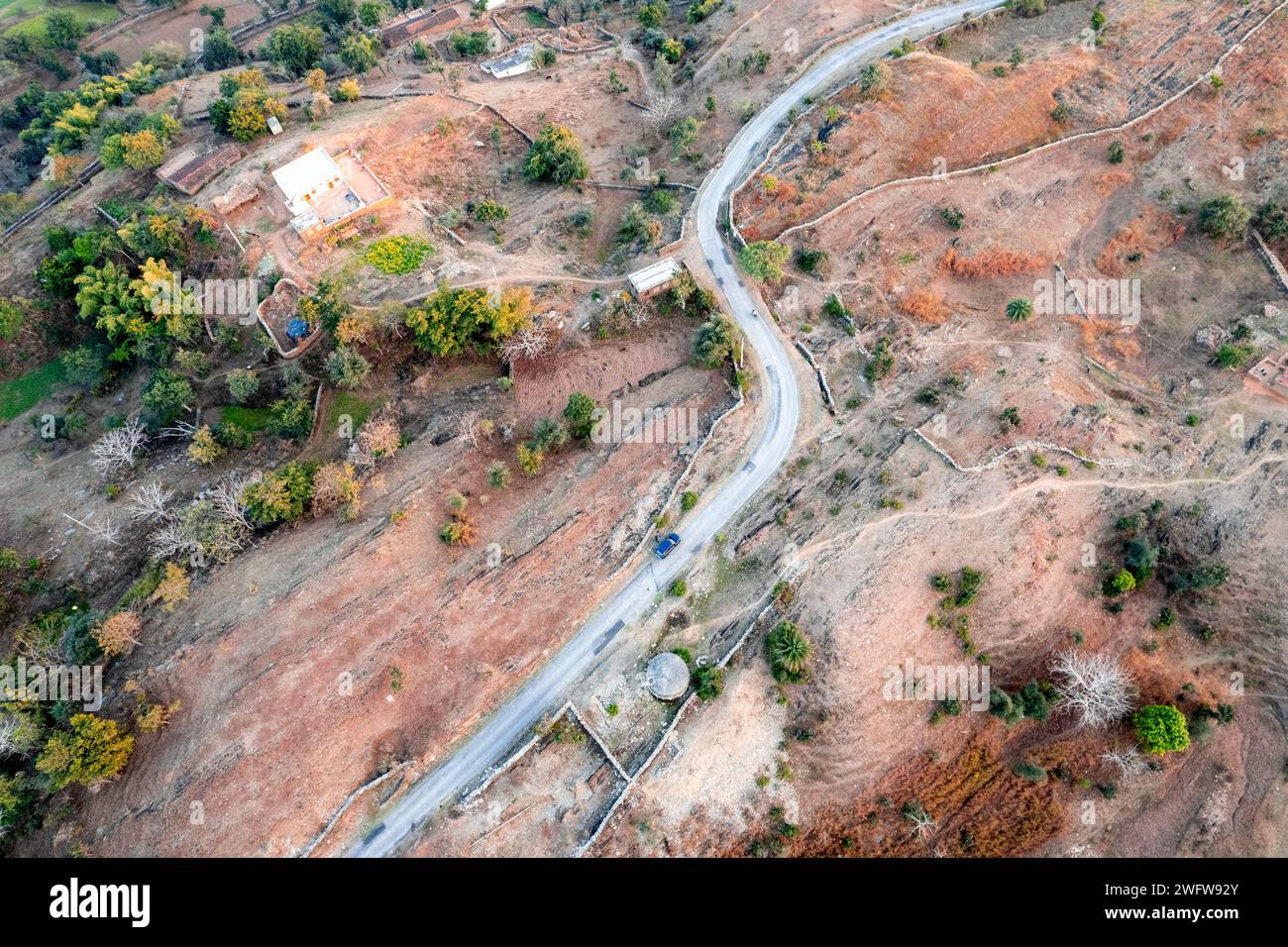 Aerial drone shot showing blue car moving on narrow country rural road ...