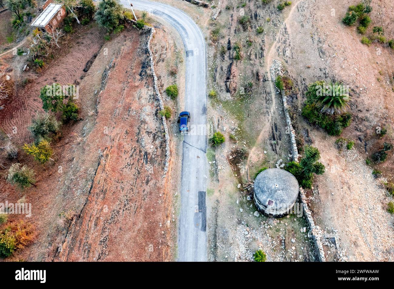 Aerial drone shot showing blue car moving on narrow country rural road ...