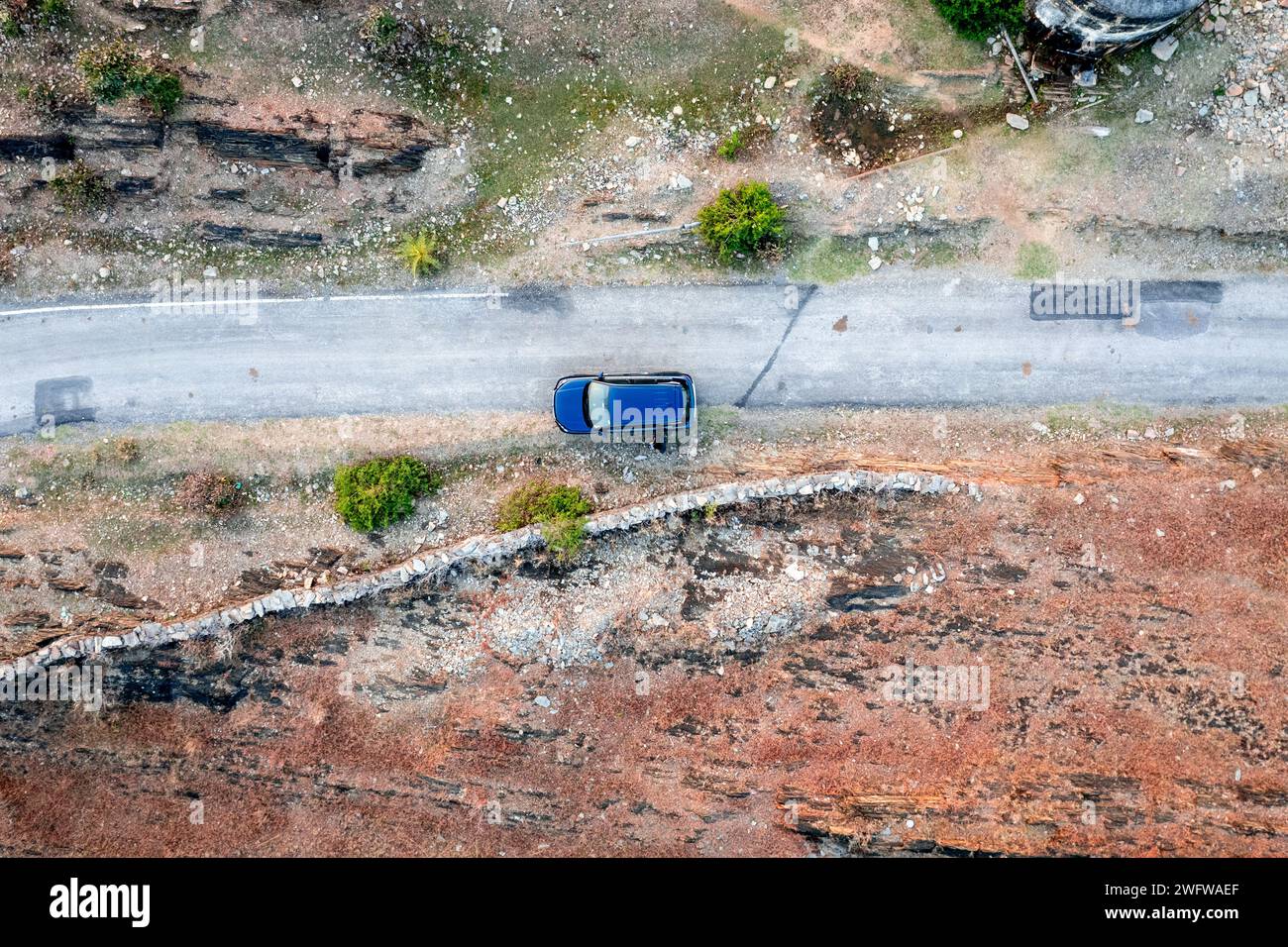 Aerial drone shot showing blue car moving on narrow country rural road ...