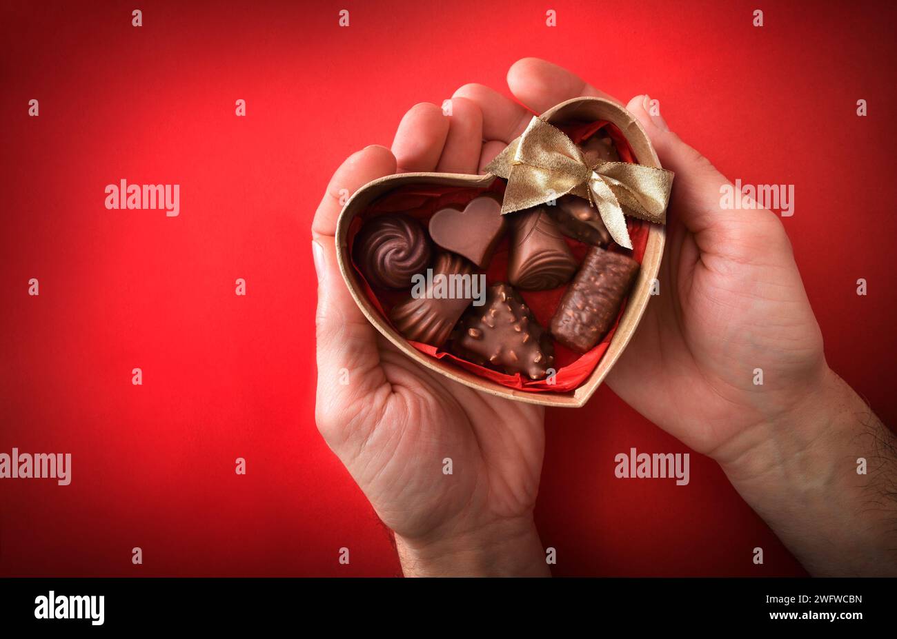 Hands holding brown heart-shaped box filled with assorted chocolates ...