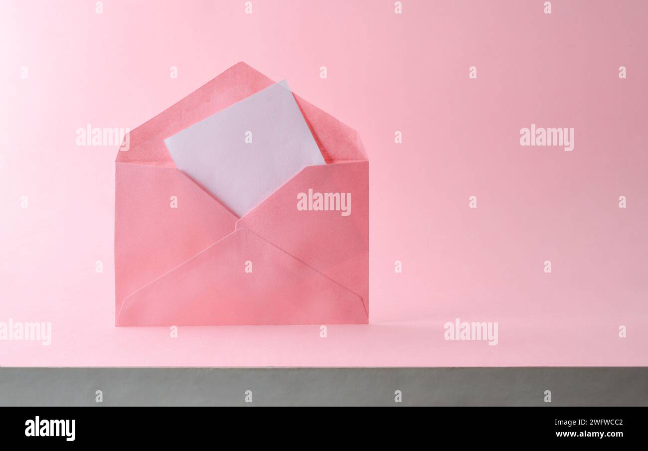 Open pink envelope with empty white sheet with heart cutouts coming out on pink textured ...