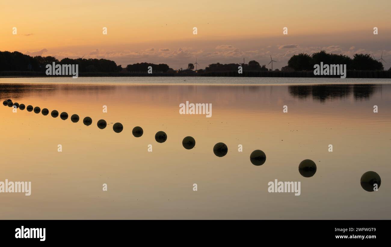 A line of buoys reclected in a calm lake during sunrise. The reflection ...
