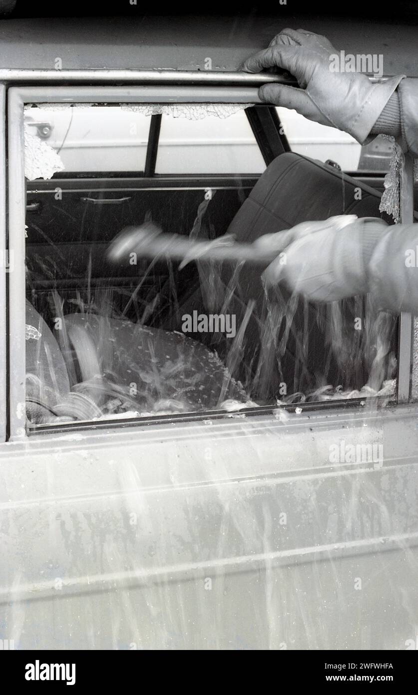 1970s, historical, a gloved car thef smashing a car window with a ...
