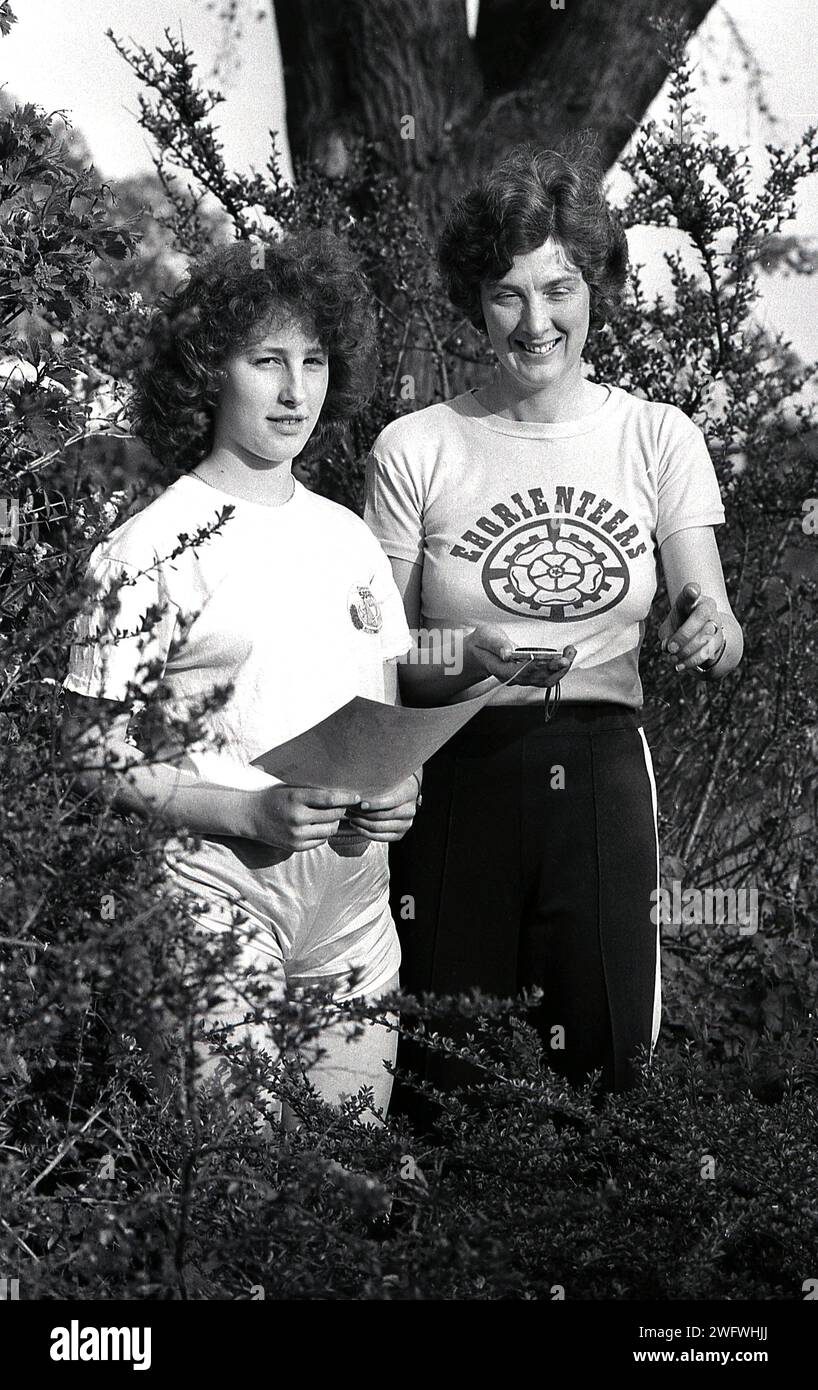 1980s, outside in woodland, a young woman, holding a small map, on an ...