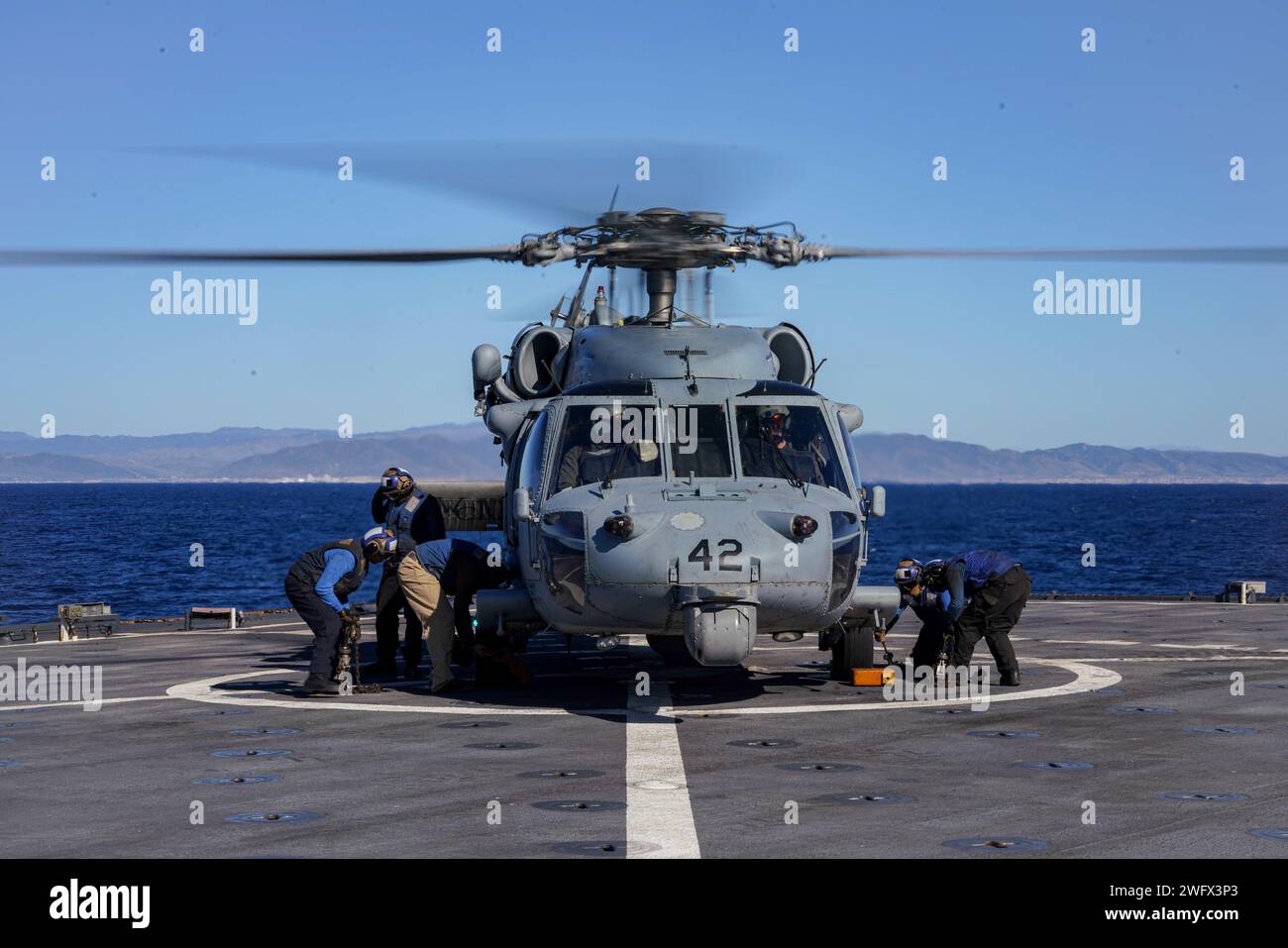 Sailors use chocks and chains to secure an SH-60S Seahawk, attached to ...