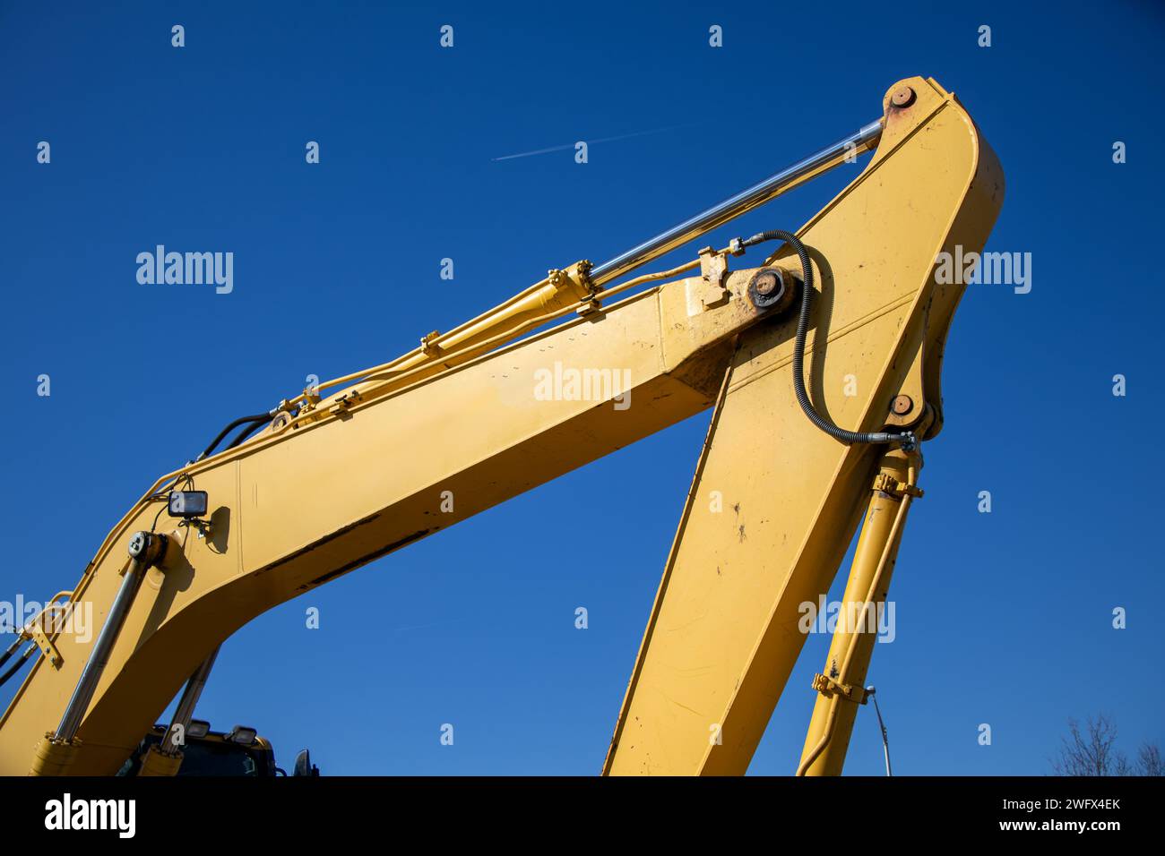 Yellow Excavator Arm with Bright Blue Sky Background and Distant Plane ...