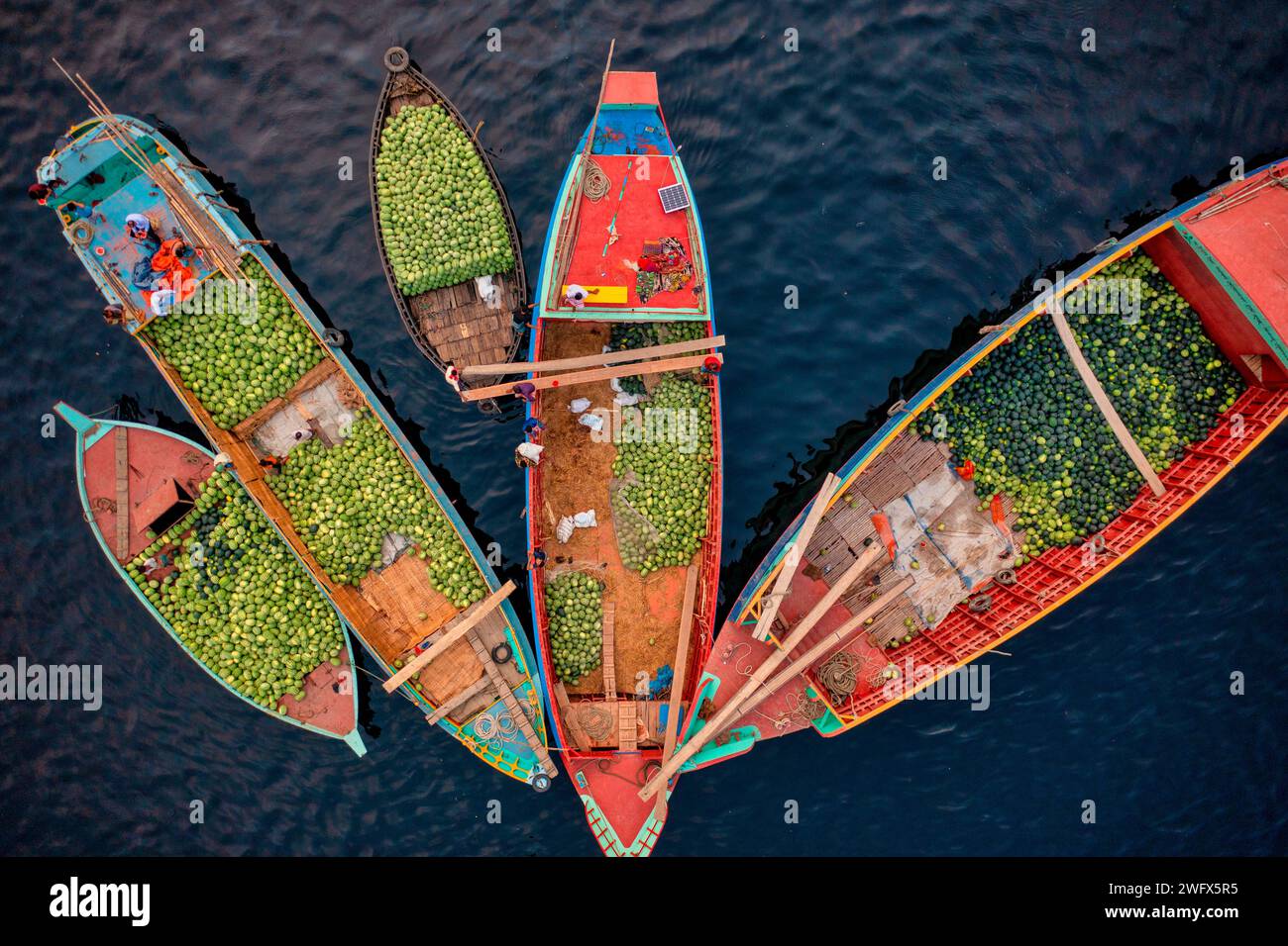 Aerial view of several small commercial boats with people unloading watermelons at Old Dhaka ...
