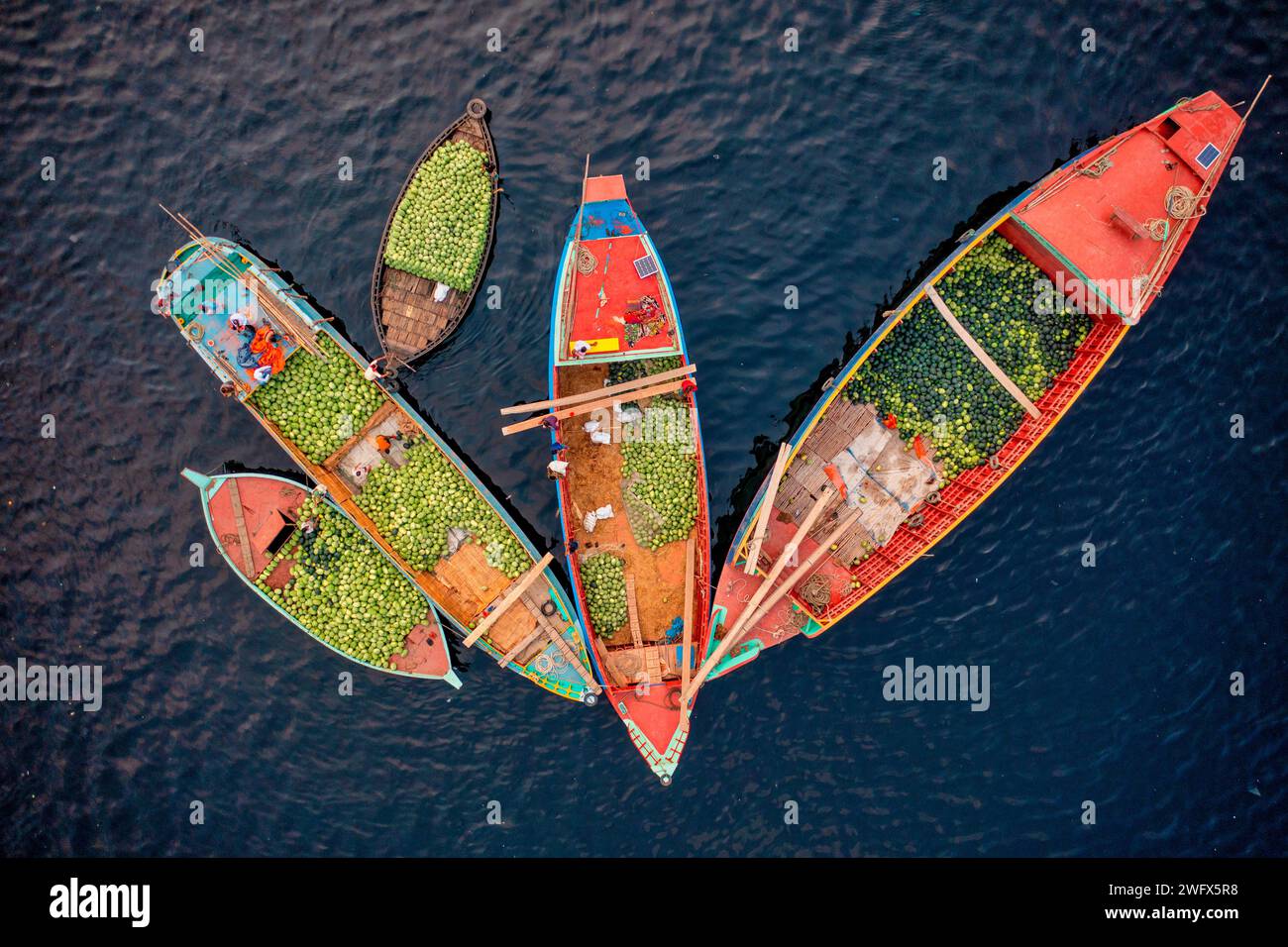 Aerial view of several small commercial boats with people unloading watermelons at Old Dhaka ...